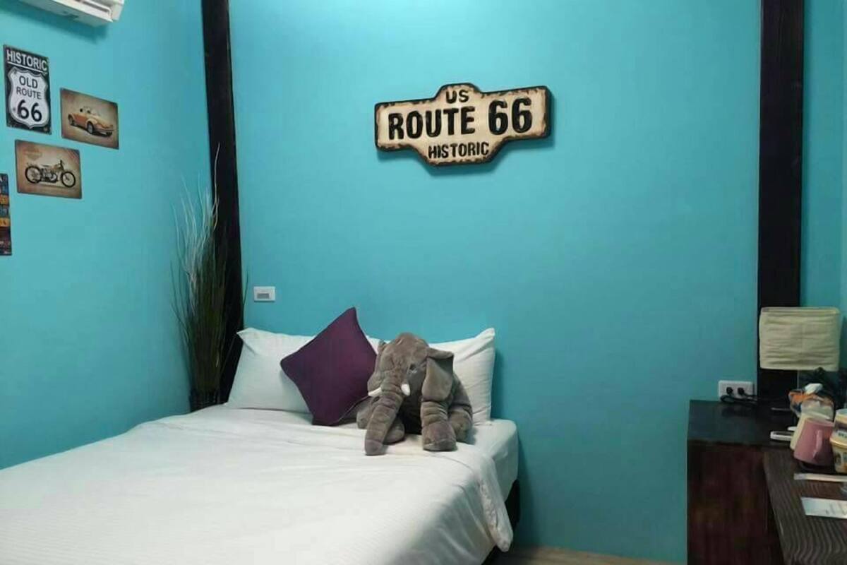 Quarto com cama, almofadas, um brinquedo de pelúcia e uma placa na parede com a inscrição 'US Route 66 Historic'.