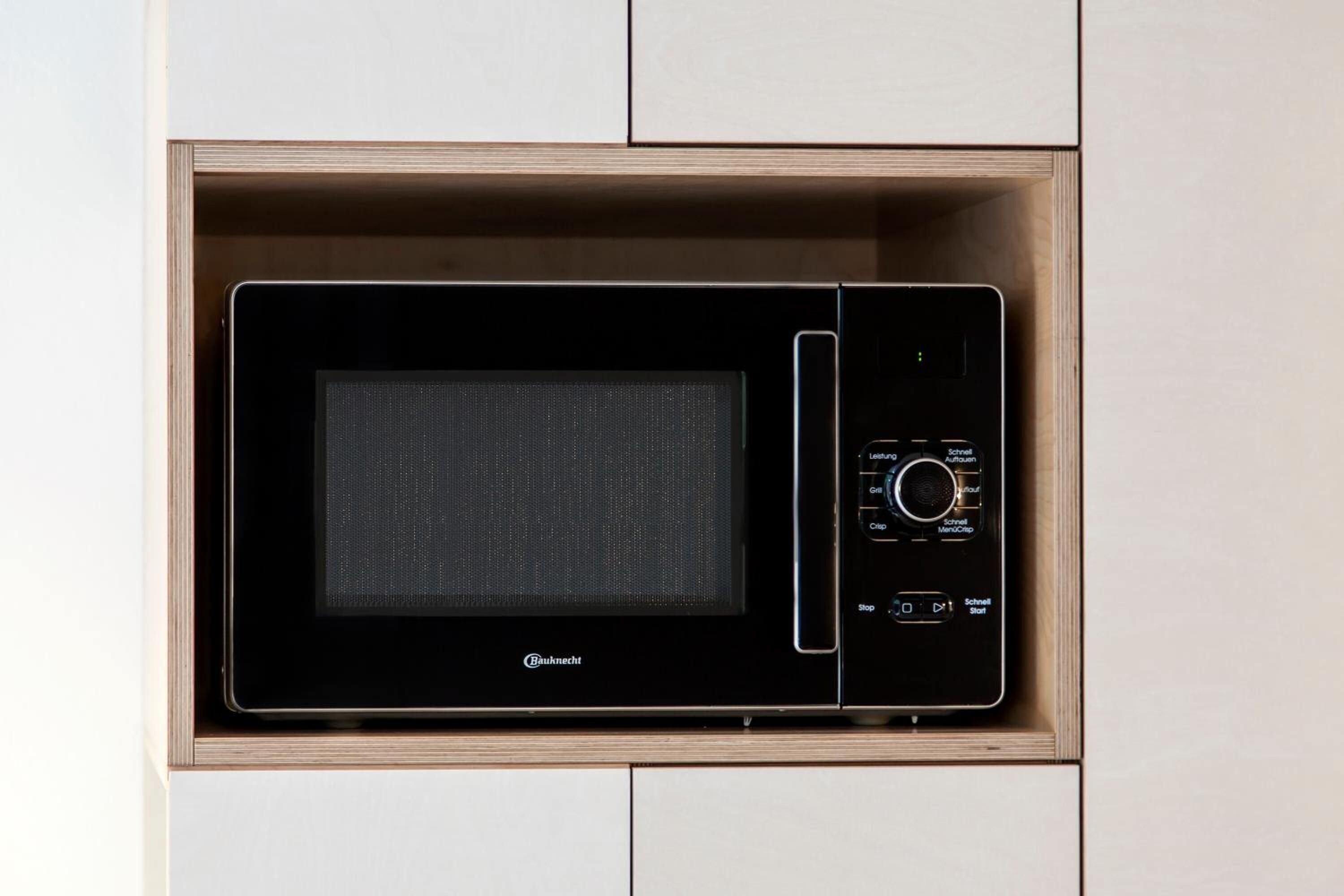 Forno de micro-ondas preto numa cozinha com armários de madeira e painel de controle no lado direito.