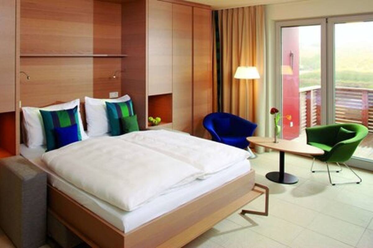 Quarto de hotel com uma cama grande, uma escrivaninha, duas cadeiras e vista para o exterior.