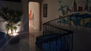 Um corredor com escadas, uma planta em vaso e um mural de pontos turísticos da cidade.