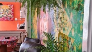 Um quarto com uma poltrona de couro preta, uma planta grande em vaso e um mural abstrato colorido na parede.