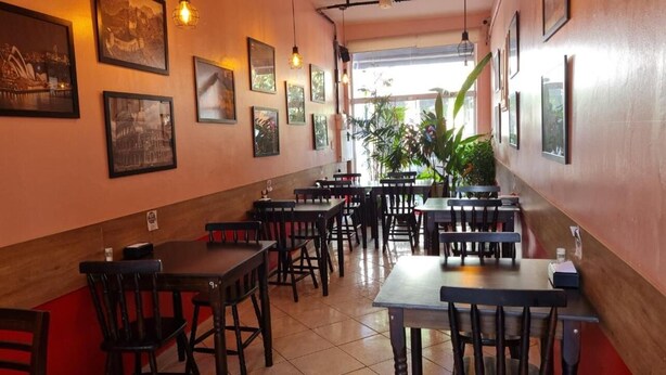 Interior de restaurante com mesas e cadeiras de madeira, quadros nas paredes e plantas em vasos.