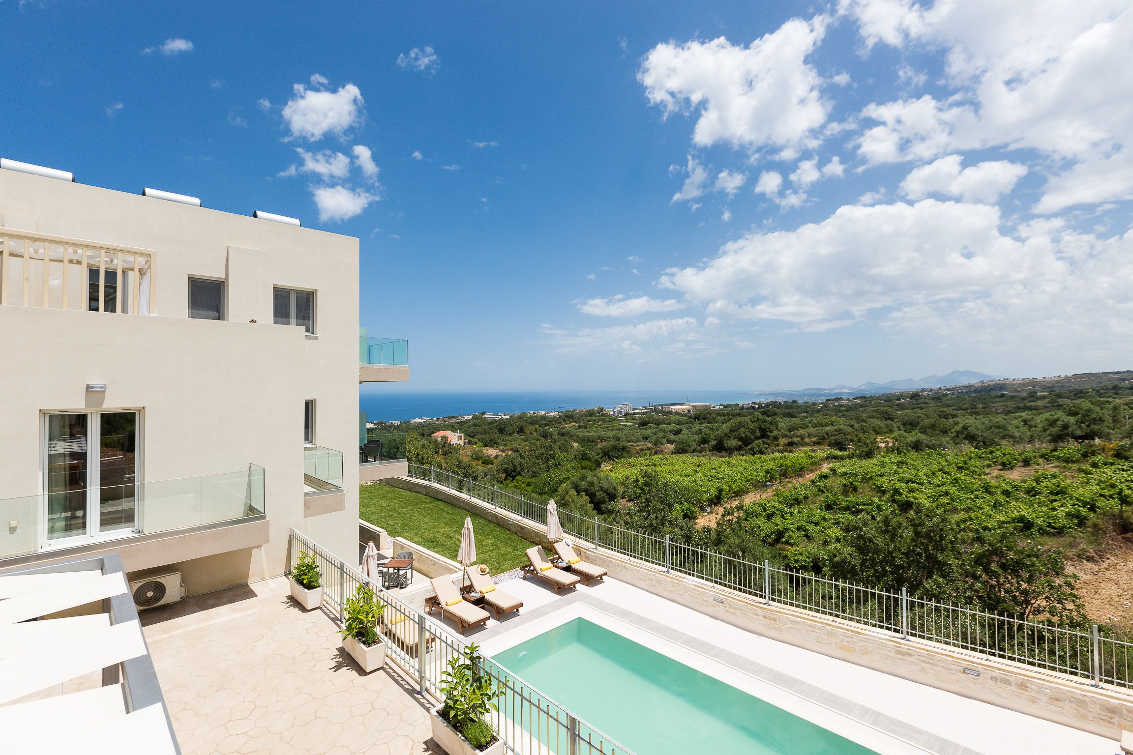 Um edifício moderno com piscina no terraço, espreguiçadeiras e uma vista panorâmica do campo.