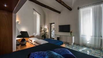 Quarto com duas camas, uma televisão, uma escrivaninha e uma janela grande com cortinas.