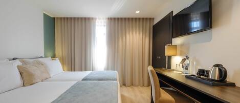 Quarto de hotel com duas camas, uma mesa, uma cadeira, uma televisão e uma janela com cortinas.