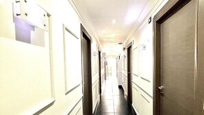 Corredor de hotel com portas em ambos os lados, piso de azulejos e uma luminária no teto.