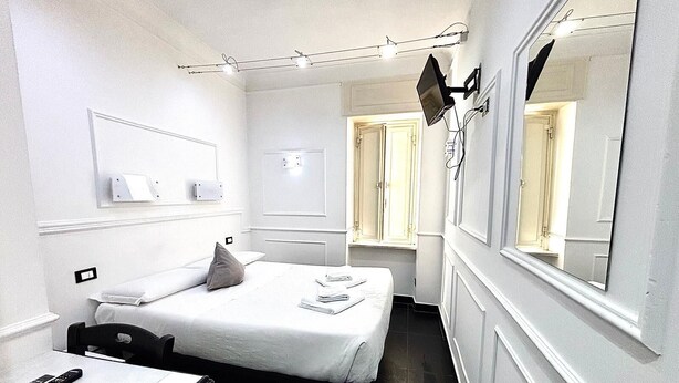 Quarto de hotel com cama, escrivaninha, espelho e janela.