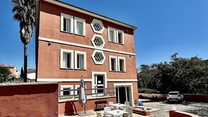 Um edifício de dois andares com fachada vermelha, várias janelas e um pátio pavimentado com mobiliário de exterior.
