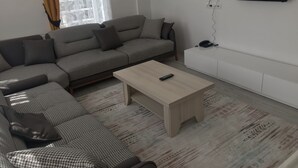 Uma sala de estar com sofá, mesa de centro e televisão na parede.