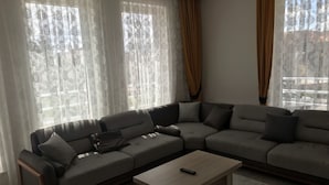 Uma sala de estar moderna com um sofá seccional grande, uma mesa de centro e janelas amplas com cortinas leves.