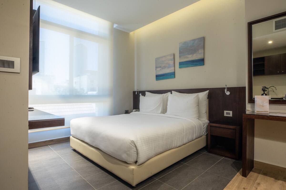 Quarto moderno com uma cama grande, mesa de cabeceira, espelho e obras de arte na parede.