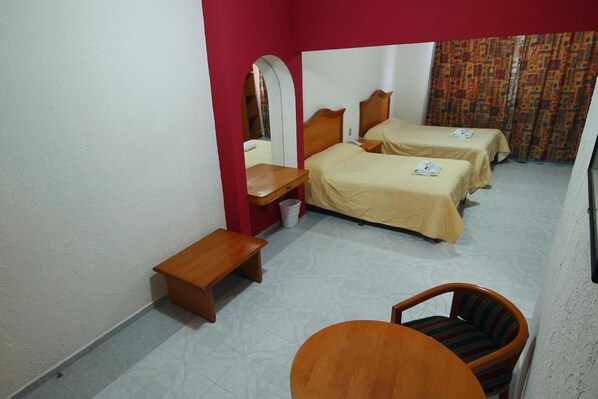 Quarto de hotel com duas camas, um pequeno banco de madeira, uma mesa redonda e uma cadeira listrada.