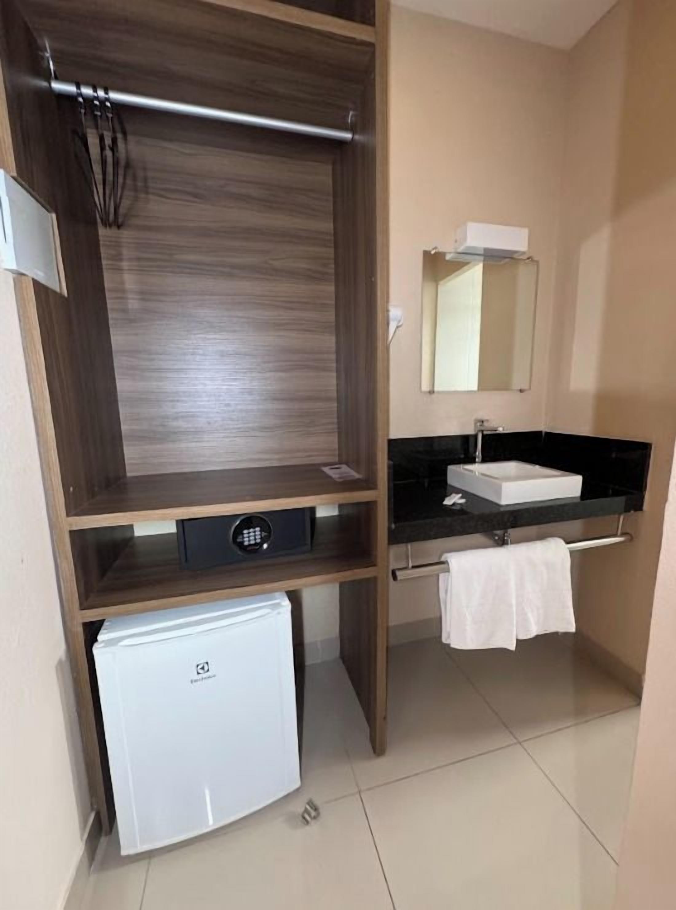 Casa de banho compacta com toucador de madeira, lavatório branco, espelho e pequeno frigorífico.