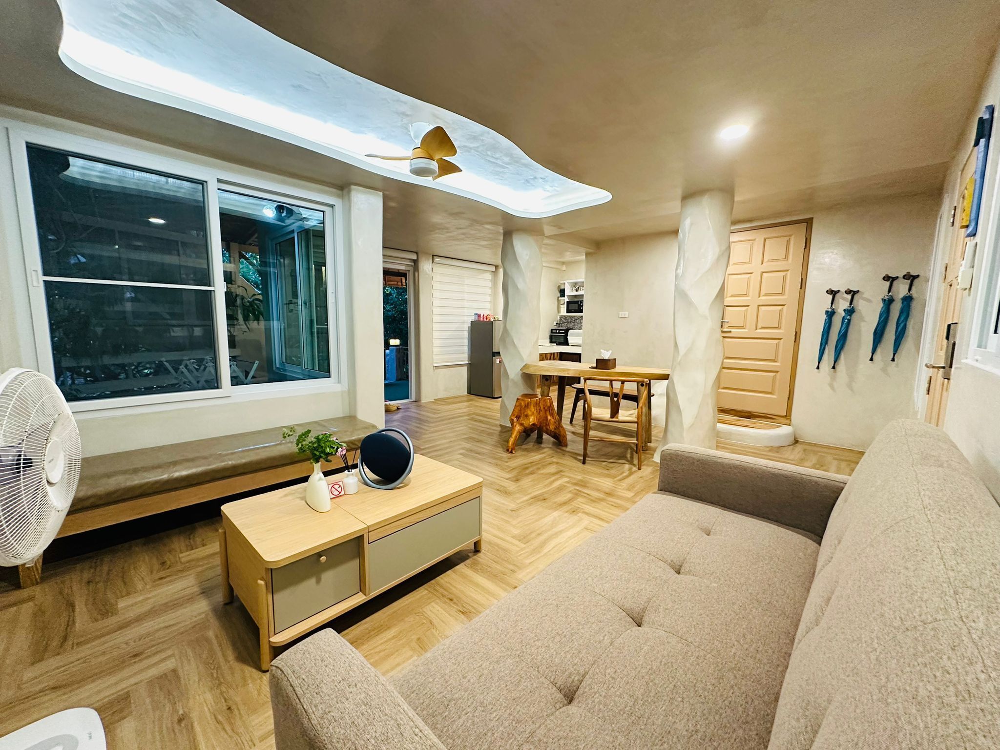 Uma sala de estar com sofá, mesa de centro de madeira, ventilador e ventoinha no teto.
