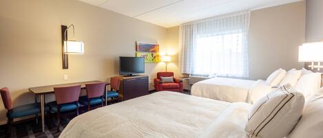 Quarto de hotel com duas camas, uma mesa com cadeiras, televisão e janela com cortinas.
