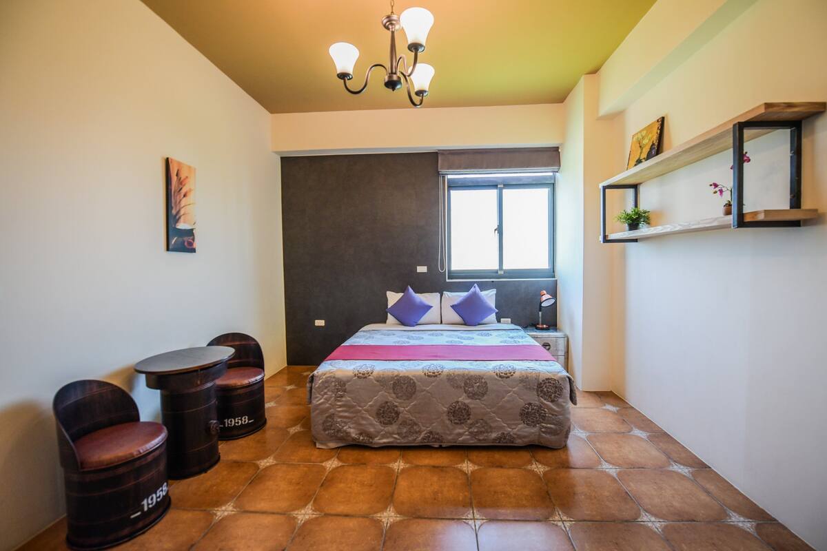 Quarto com cama, janela, lustre, prateleira com planta e porta.