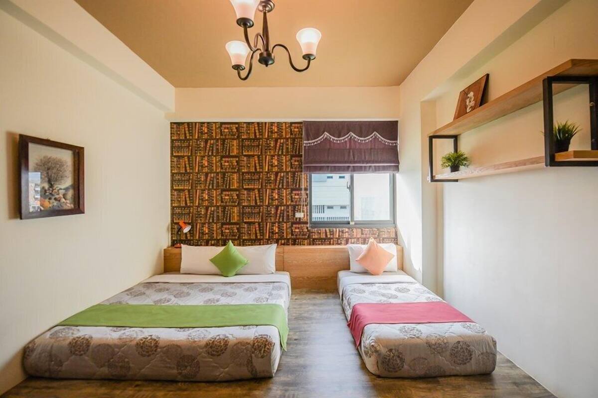 Quarto com duas camas, estante de livros, candelabro e janela com cortina.