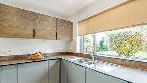 Uma cozinha moderna com armários azul claro, um armário superior de madeira, uma pia de aço inoxidável e uma janela com vista para o verde.