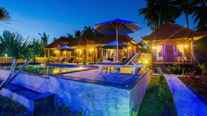Resort com piscina, espreguiçadeiras, guarda-sóis e área de estar coberta.