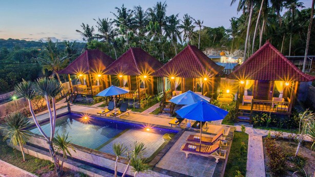 Um resort com várias bangalôs sobre a água, uma piscina e vegetação tropical exuberante.