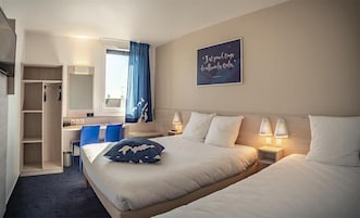 Quarto de hotel com cama, mesas de cabeceira, escrivaninha, cadeira, guarda-roupa e janela com cortinas.