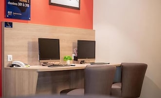 Uma receção com dois monitores de computador, um telefone e uma pequena planta.