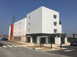 Um edifício moderno com telhado plano, entrada destacada e um hidrante na calçada.