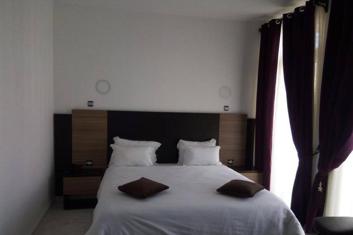 Quarto de hotel com uma cama grande, duas mesas de cabeceira e uma janela com cortinas.