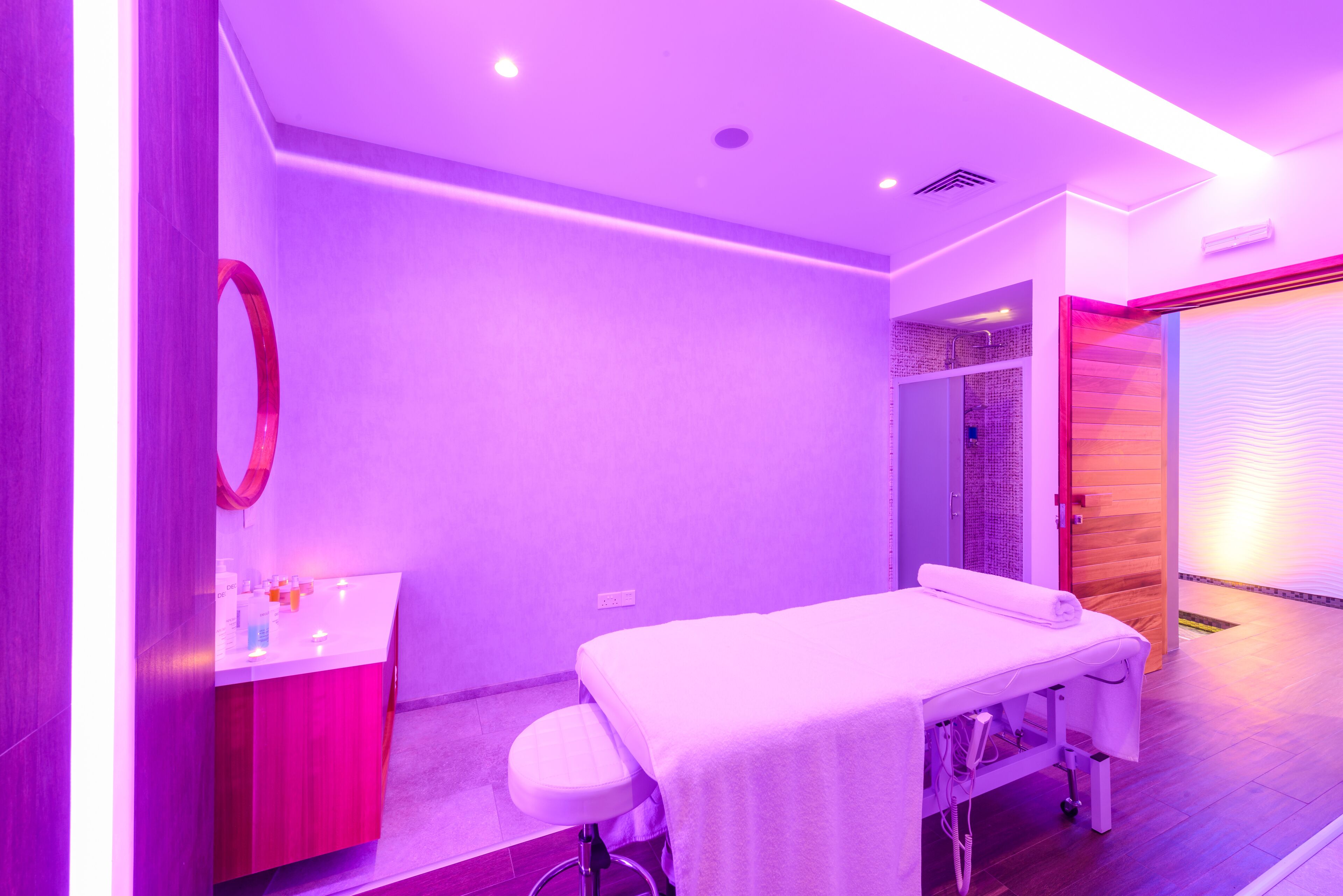 Uma sala de spa moderna, com balcão de recepção, mesa de massagem e porta de madeira.
