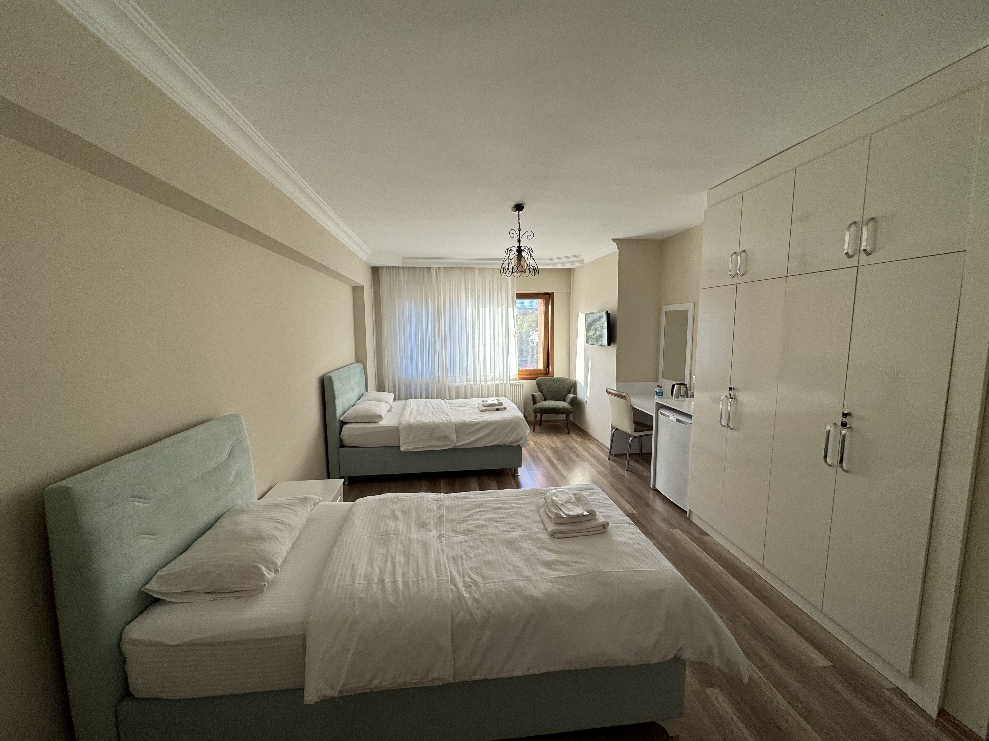 Quarto de hotel com duas camas, uma escrivaninha, um guarda-roupa e uma televisão.