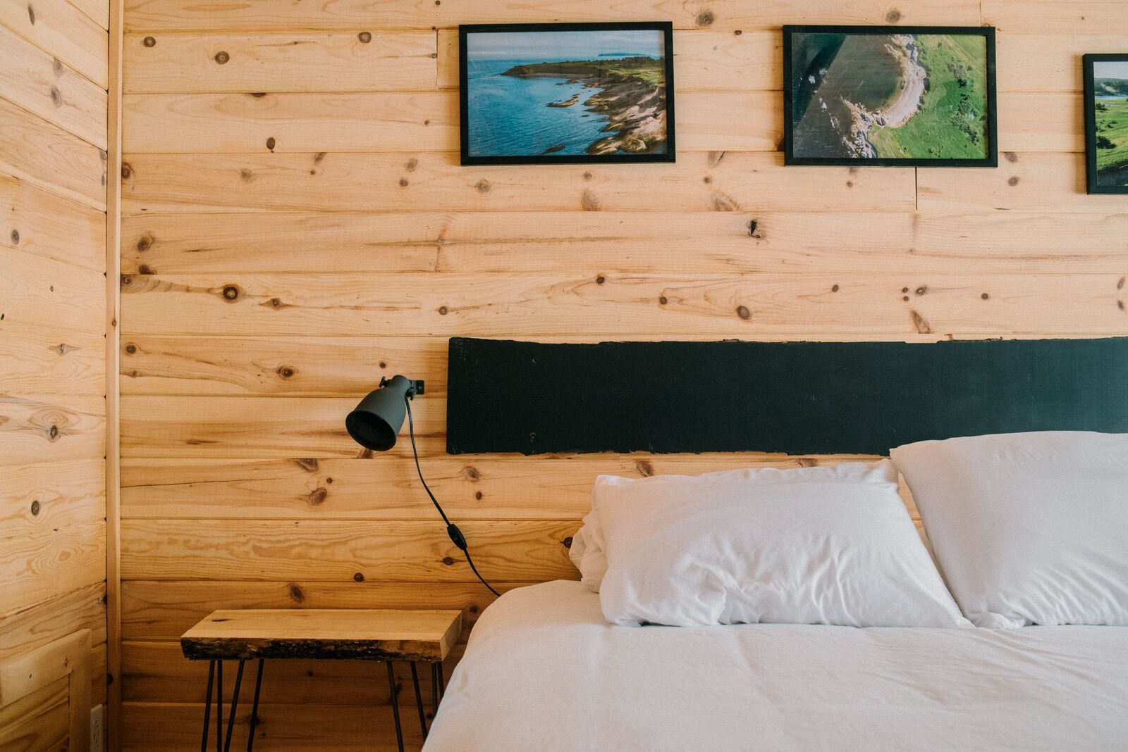Quarto de cabana de madeira com uma cama, um criado-mudo e três quadros na parede.