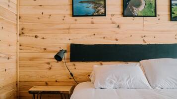 Quarto de cabana de madeira com uma cama, um criado-mudo e três quadros na parede.
