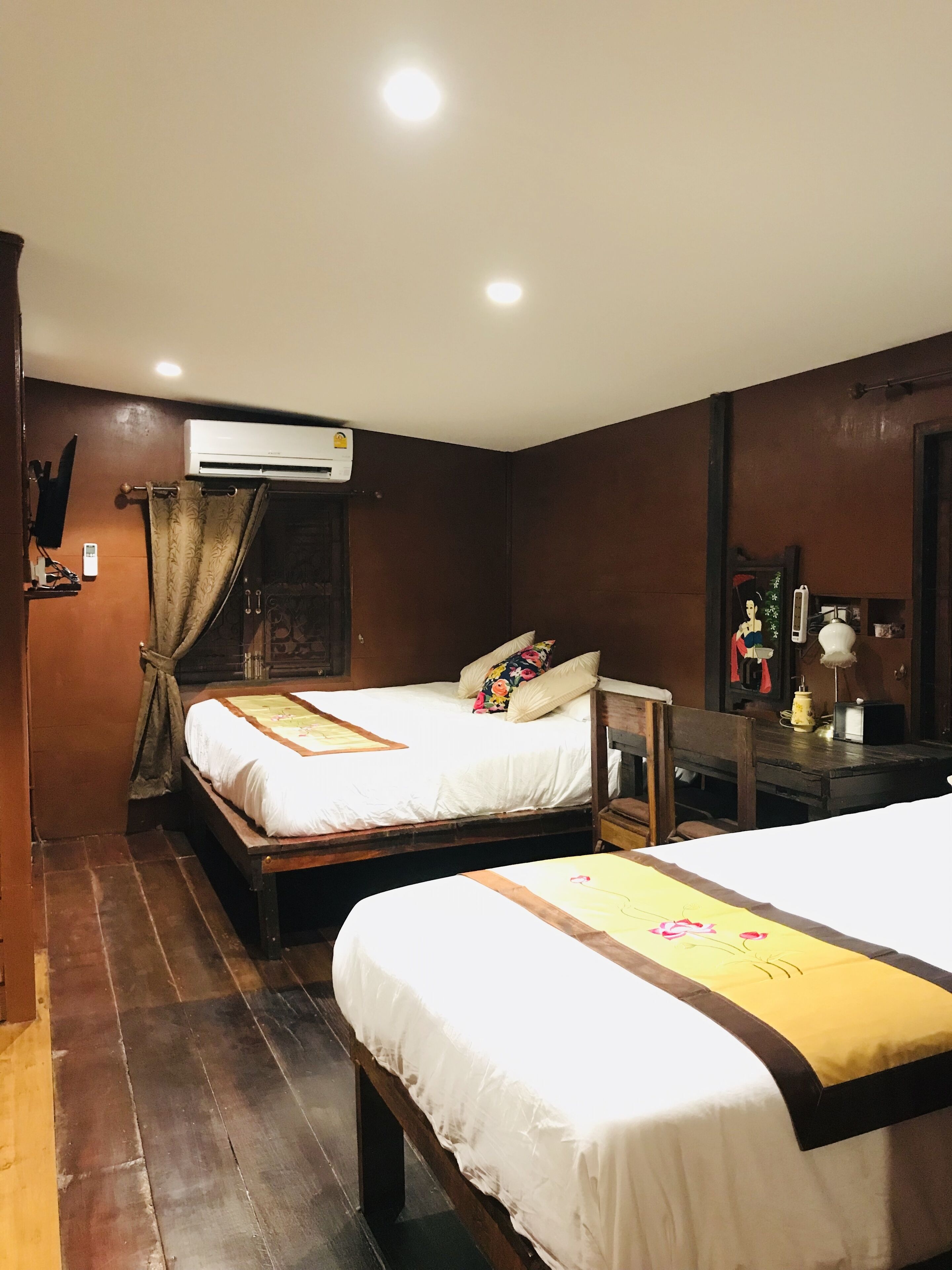 Quarto de hotel com duas camas, piso de madeira, ar condicionado, uma mesa pequena e um espelho.