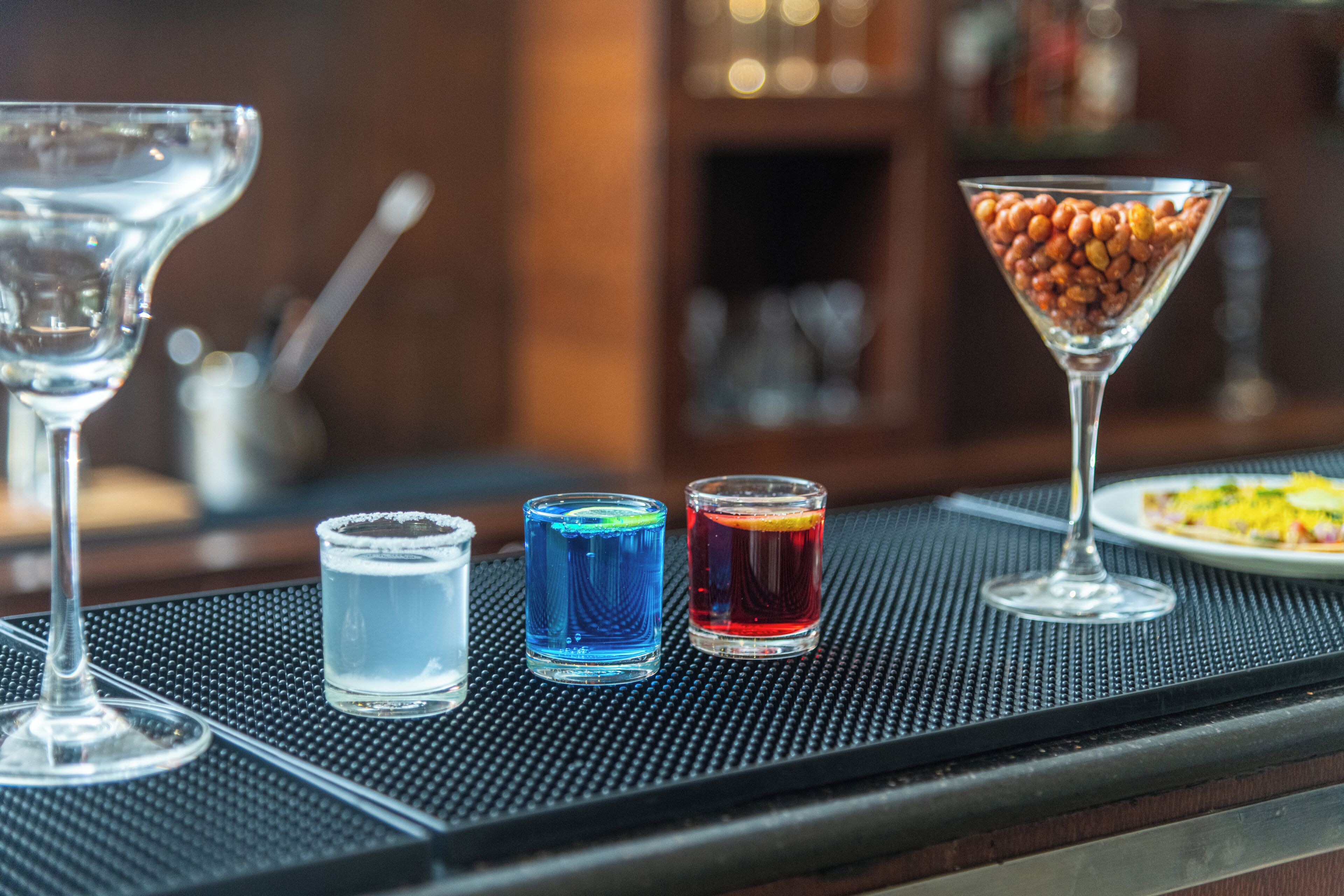 Uma área de bar com diversos copos de bebidas e um copo de martini com castanhas.