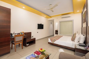 Quarto de hotel com cama, escrivaninha, cadeira, televisão e ventilador de teto.