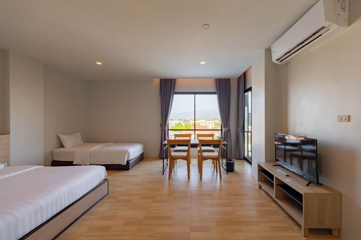Quarto de hotel com cama, televisão, mesa de jantar e cadeiras, e uma janela grande.