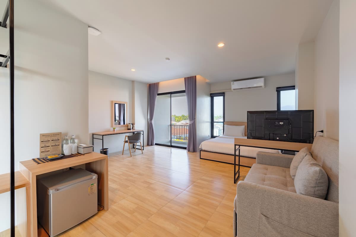 Quarto de hotel moderno com cama, escrivaninha, cadeira, mini-geladeira, televisão e varanda com cortinas.