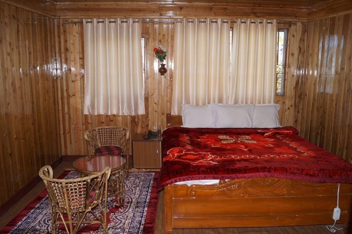 Quarto com painéis de madeira, uma cama, uma mesinha e duas cadeiras de vime.