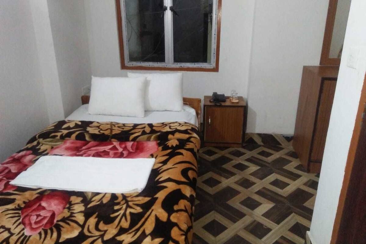Quarto com cama, mesa de cabeceira, guarda-roupa e janela.