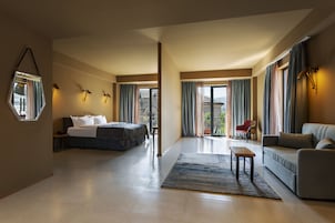 Um quarto de hotel espaçoso com uma cama grande, um sofá, uma mesa pequena e vista para o exterior através de janelas amplas.