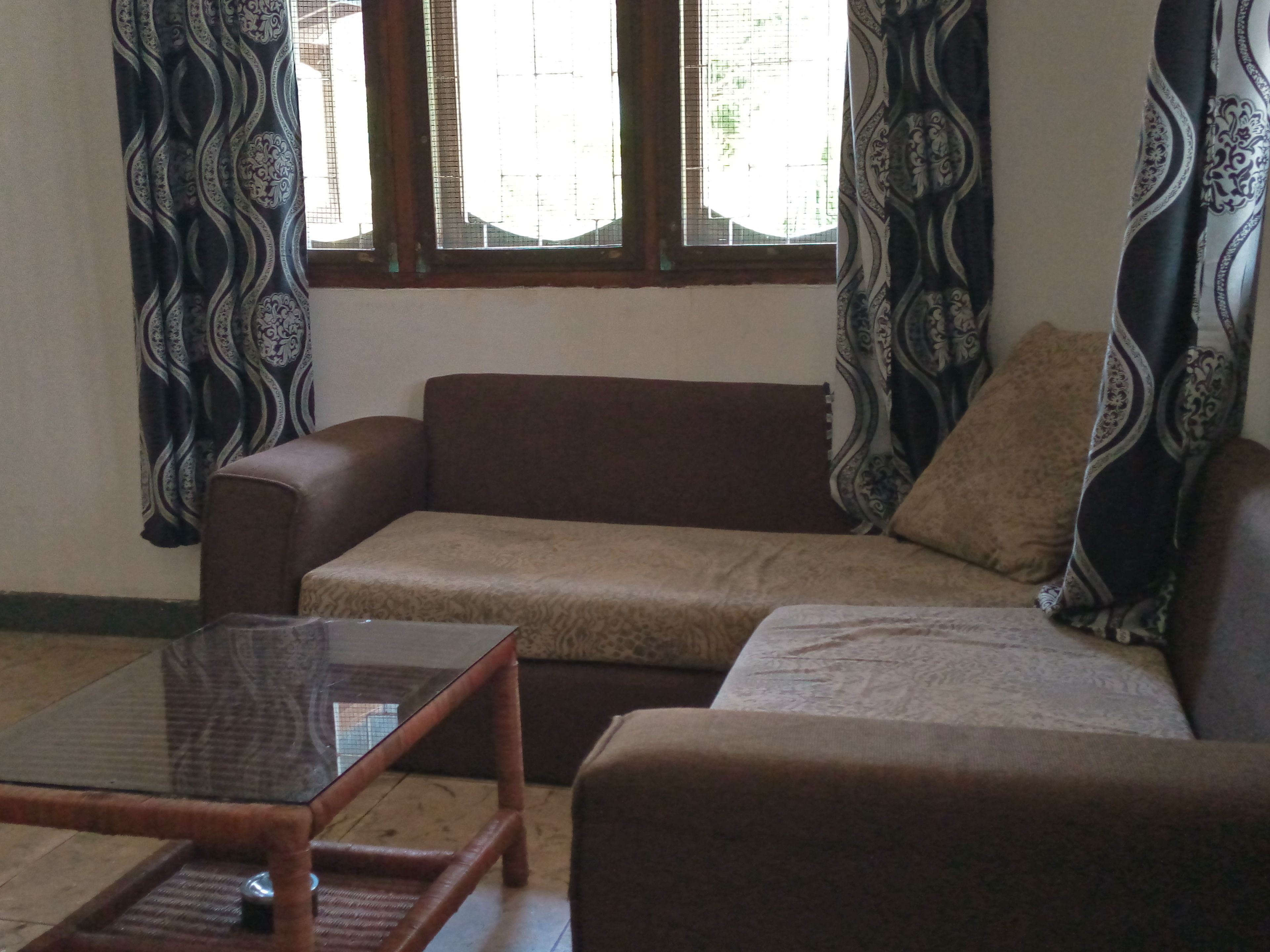 Uma sala de estar com um sofá marrom, uma mesa de centro de madeira e cortinas estampadas.