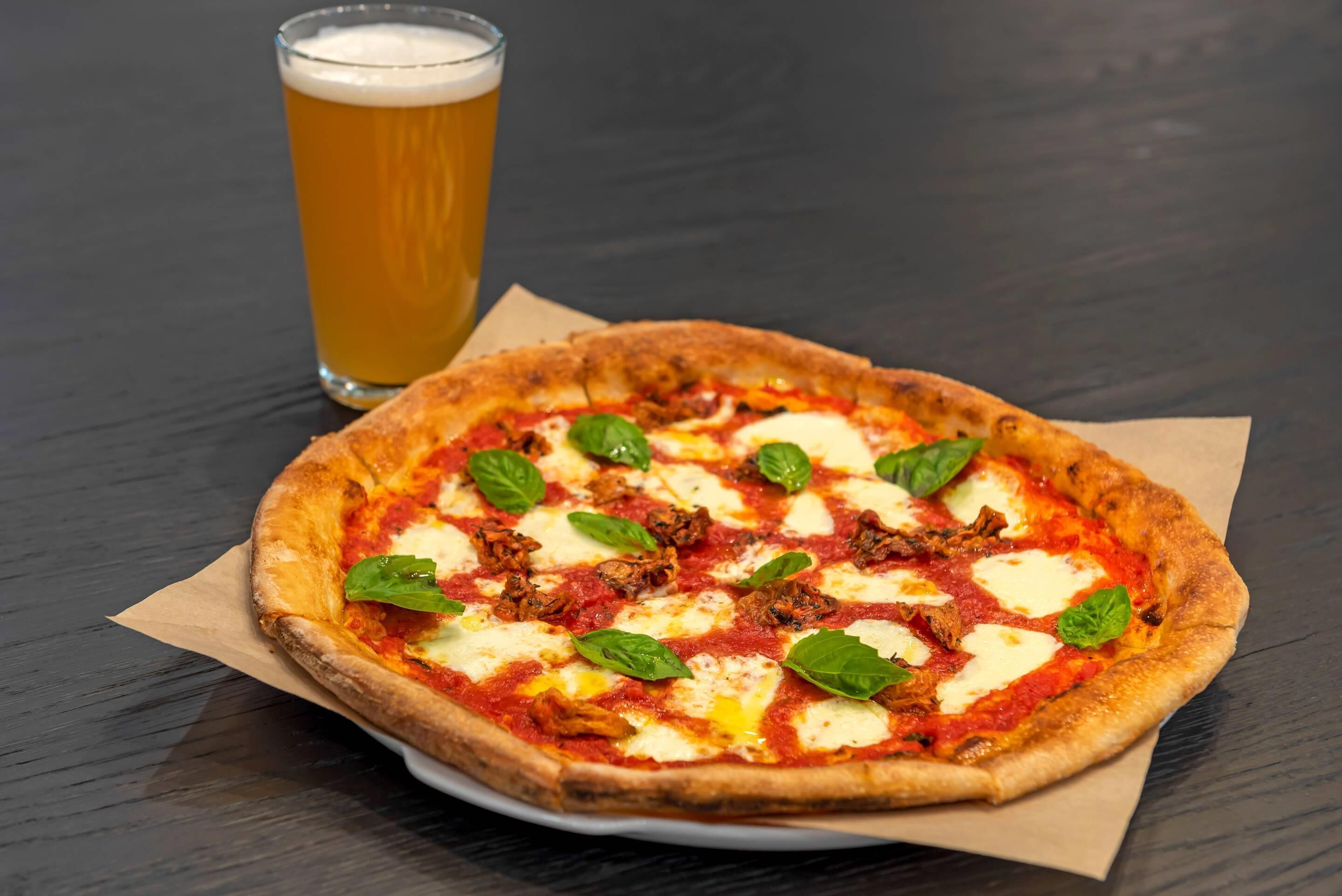 Pizza com cobertura e um copo de cerveja sobre uma mesa.