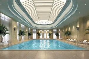 Piscina interna com teto skylight, cercada por espreguiçadeiras e plantas em vasos.
