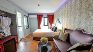 Quarto de hotel com uma cama, área de estar com sofá, mesa de centro e guarda-roupa.