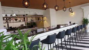 Uma área de bar com um balcão comprido, banquetas pretas e luminárias geométricas pendentes.