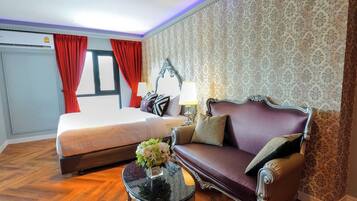Quarto de hotel com cama, sofá, mesa com flores e papel de parede estampado.