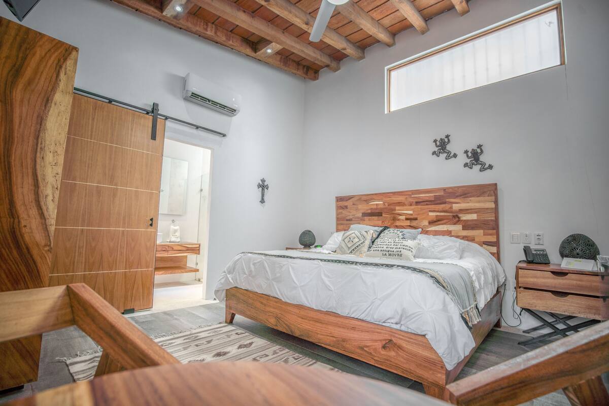 Quarto com cama de madeira, mesa de cabeceira, escrivaninha e guarda-roupa.