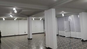Um quarto espaçoso com piso de azulejos, paredes brancas e uma grande janela com cortinas.