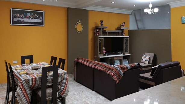 Uma sala de jantar com mesa posta para quatro pessoas, um sofá e um rack de televisão.