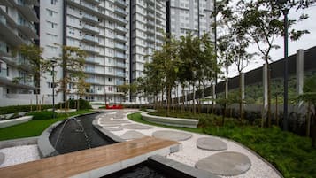 Um edifício residencial moderno com um jardim ajardinado, apresentando um espelho d'água, caminhos e vegetação.